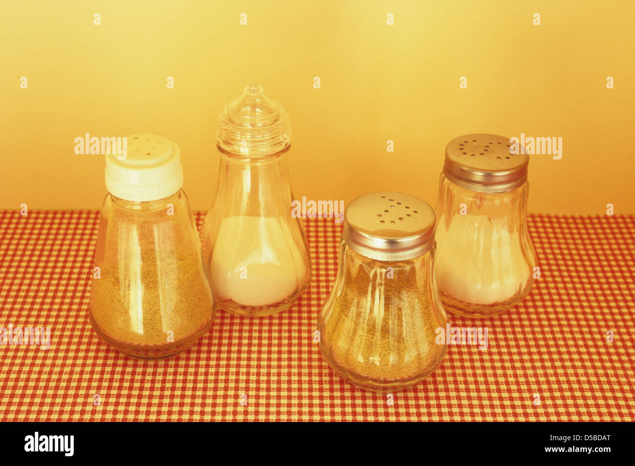 Two pairs of salt and pepper cruets on shelf covered with red gingham ...
