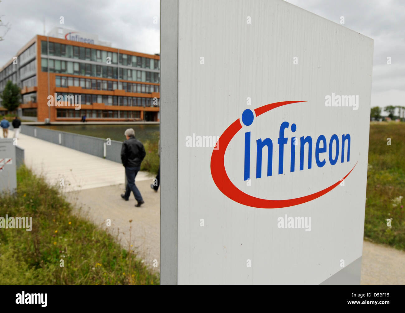 Infineon employees walk past the company logo in front of the company ...