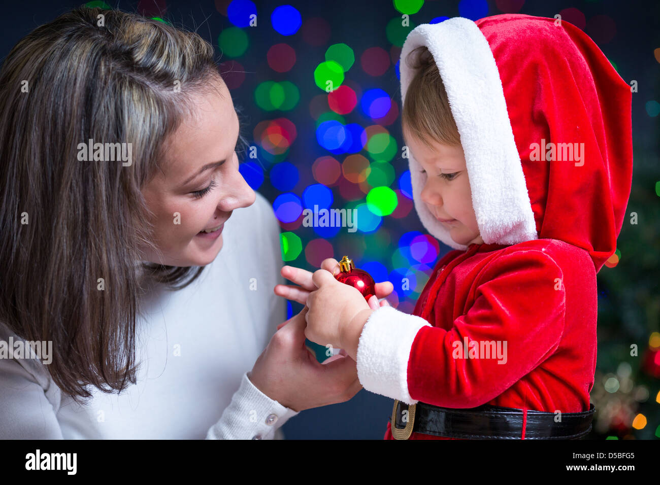 baby in Santa Claus clothes and mother on bright festive background ...