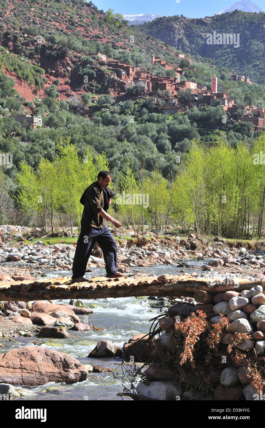 Man crosses a bridge over the river Oued Ourika that cascades down the ...