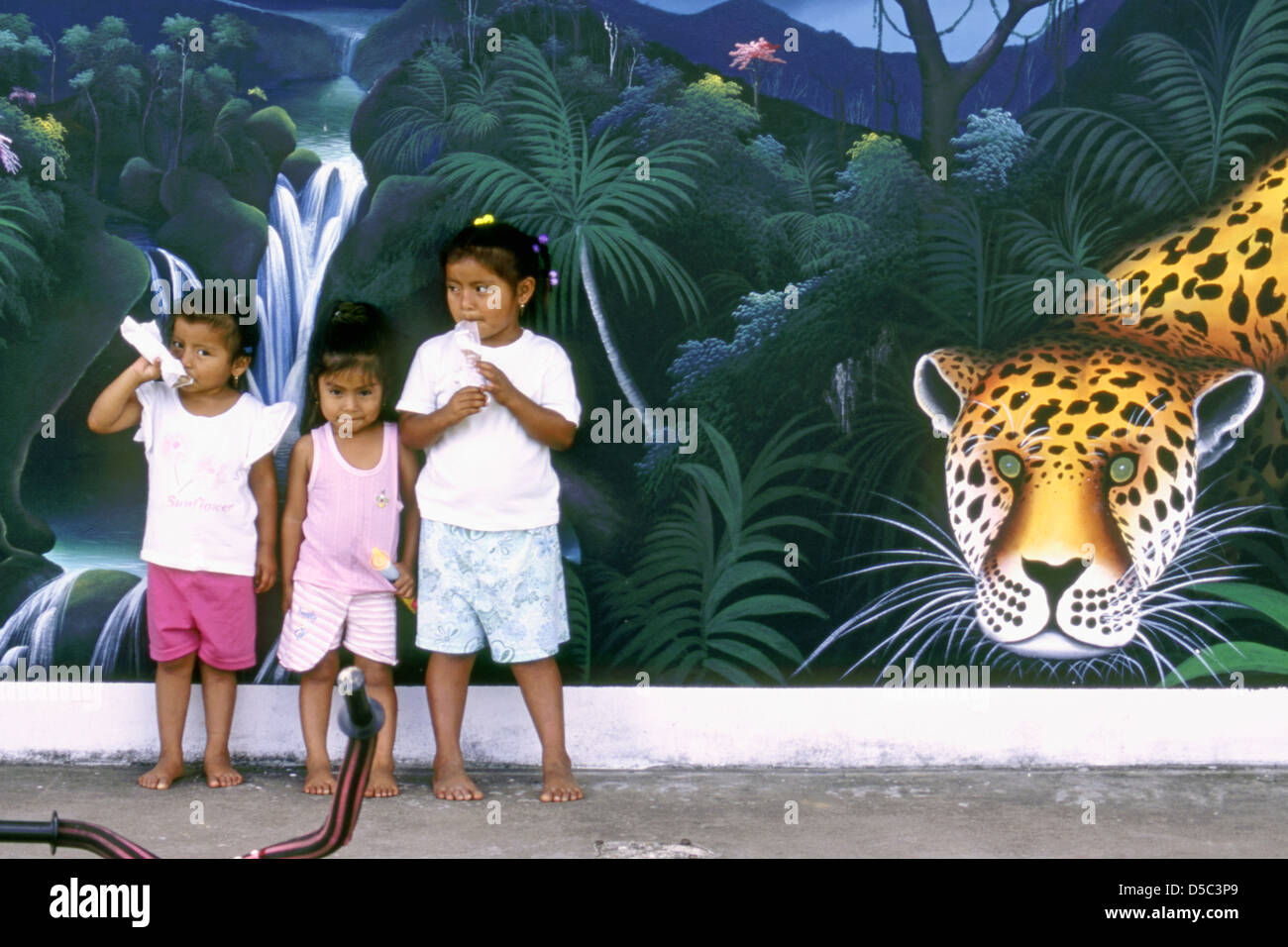 Three maya children standing in front of a jaguar mural outside belize ...