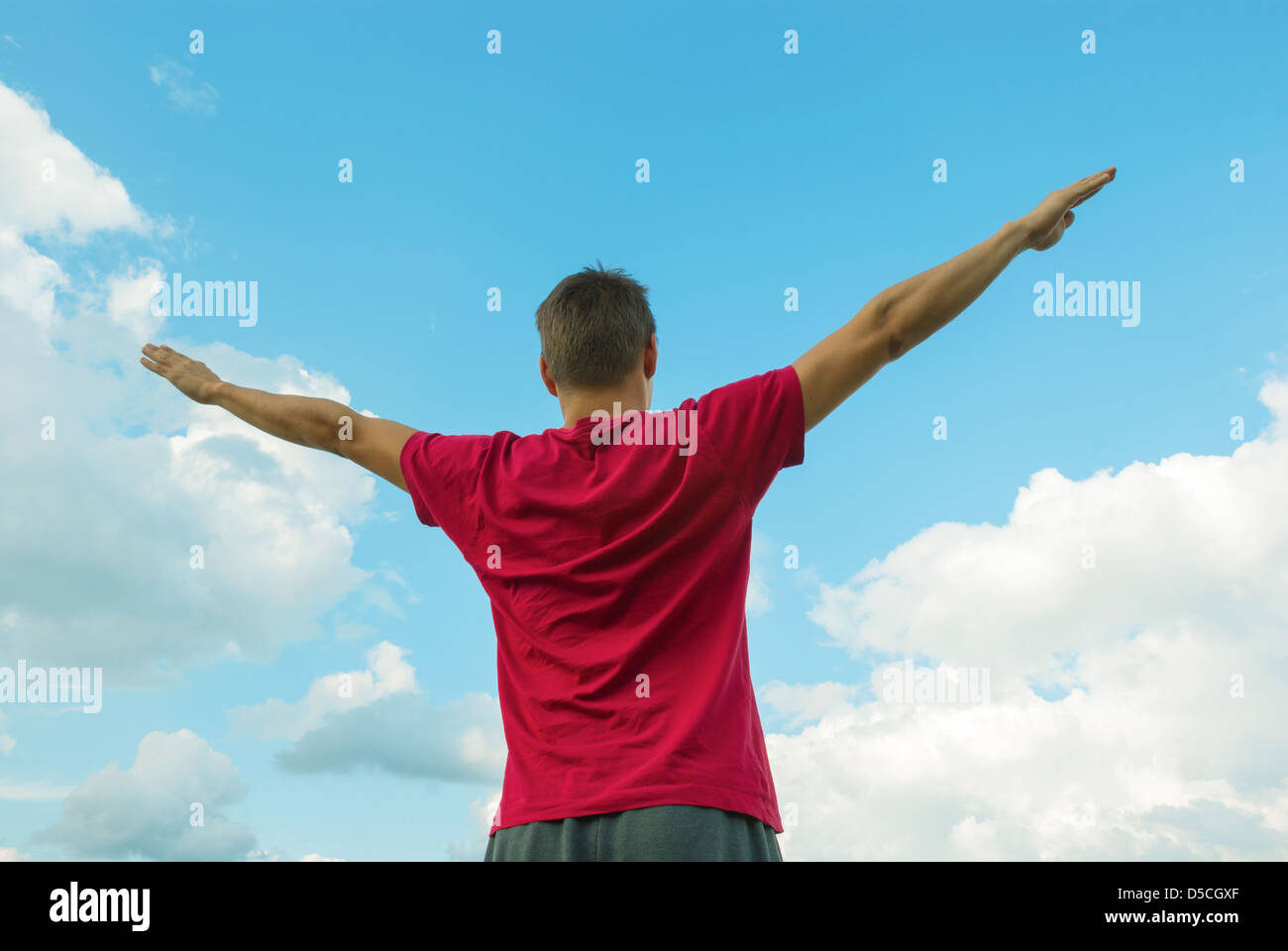 Young man staying with raised hands against blue sky Stock Photo - Alamy