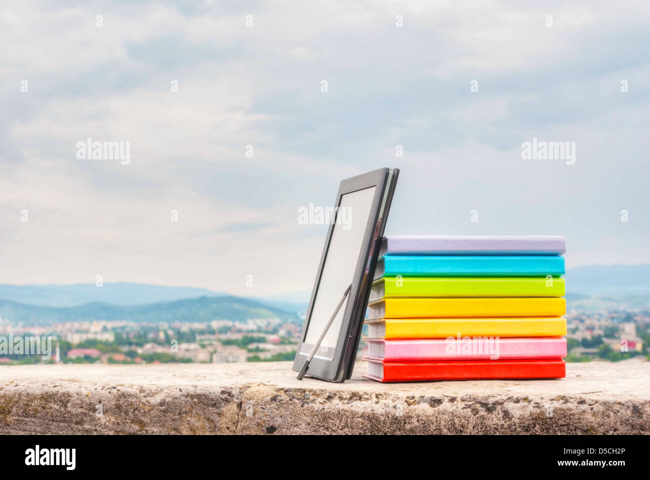 Stack of colorful books with electronic book reader against blue sky ...