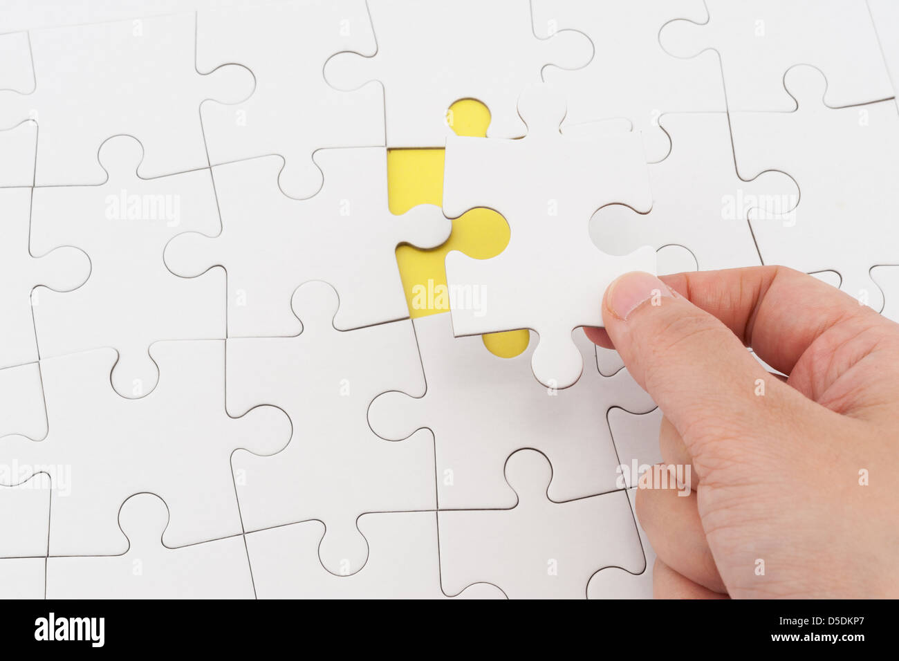 Hand holding puzzle piece and inserting it into group of white paper ...