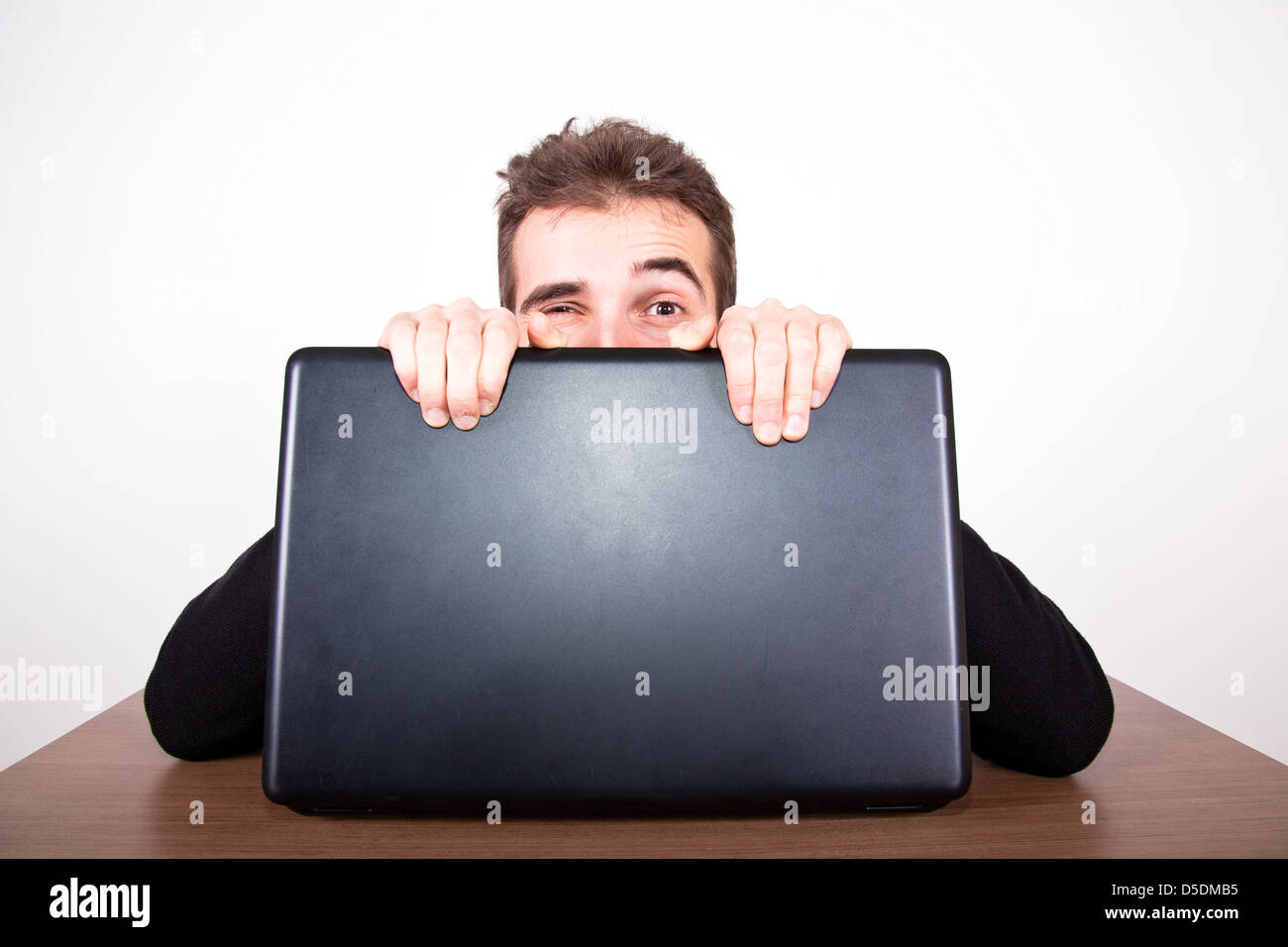 Young man sitting behind a laptop winking with one eye and gripping ...