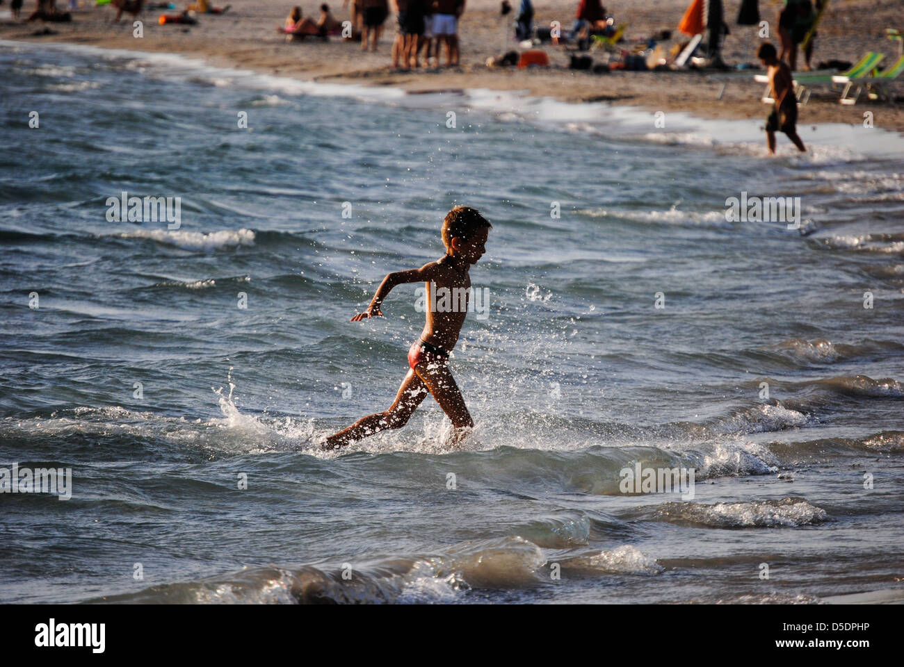 A boy running through the water towards the shore in Sardinia Stock ...