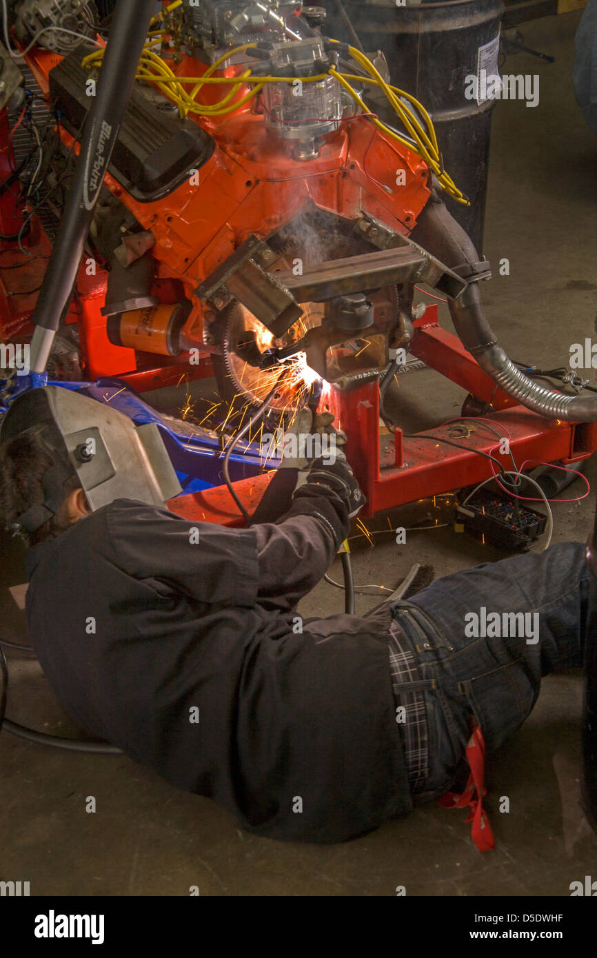 A teen boy arc welds an engine support in a high school auto shop class ...