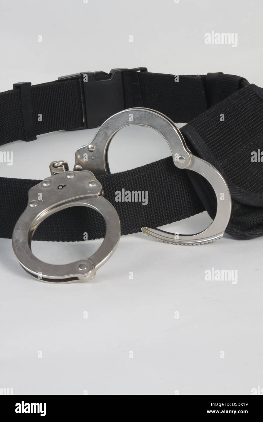 Metal handcuffs draped over a black utility belt against a light ...