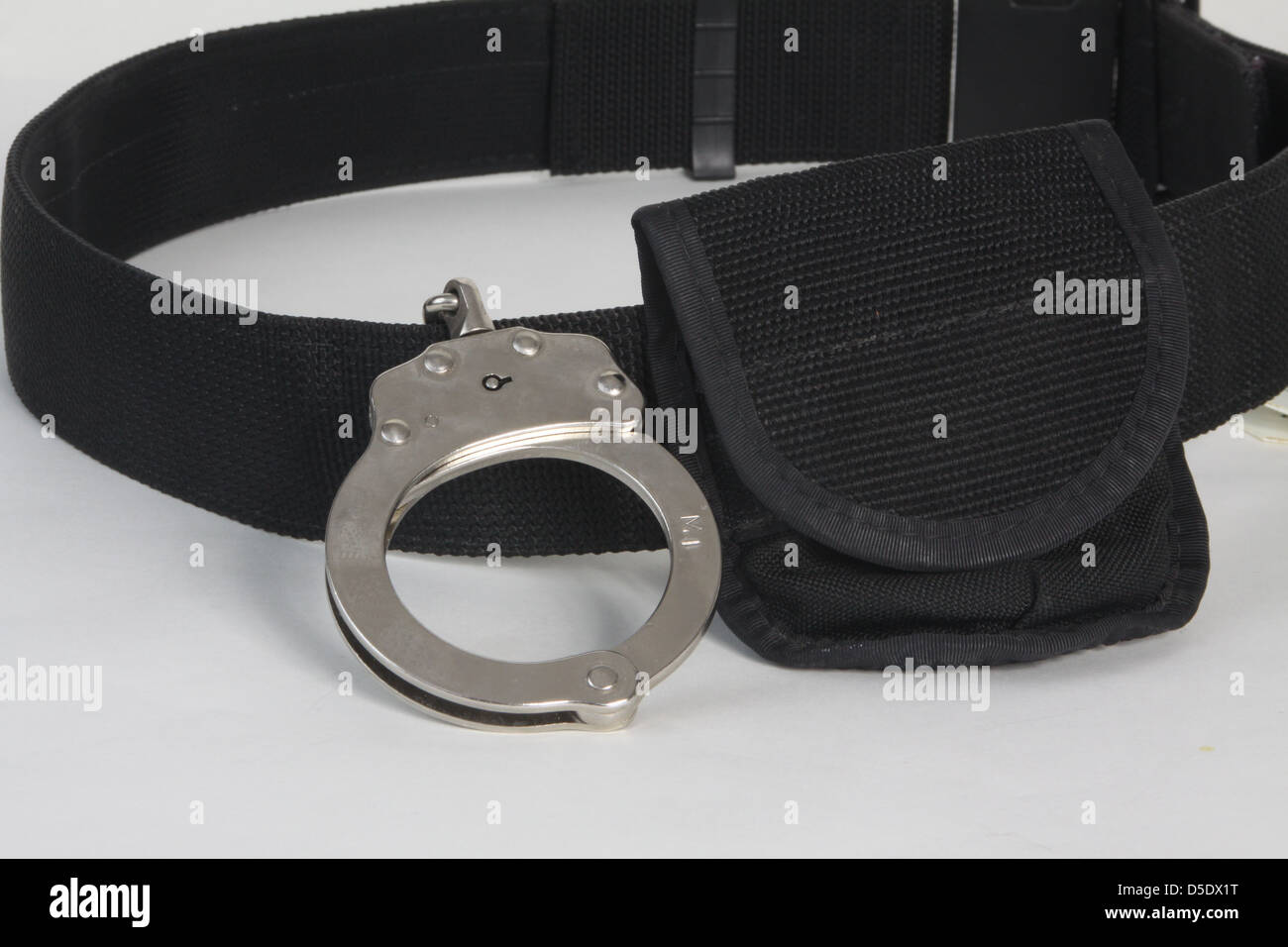 Metal handcuffs draped over a black utility belt against a light ...