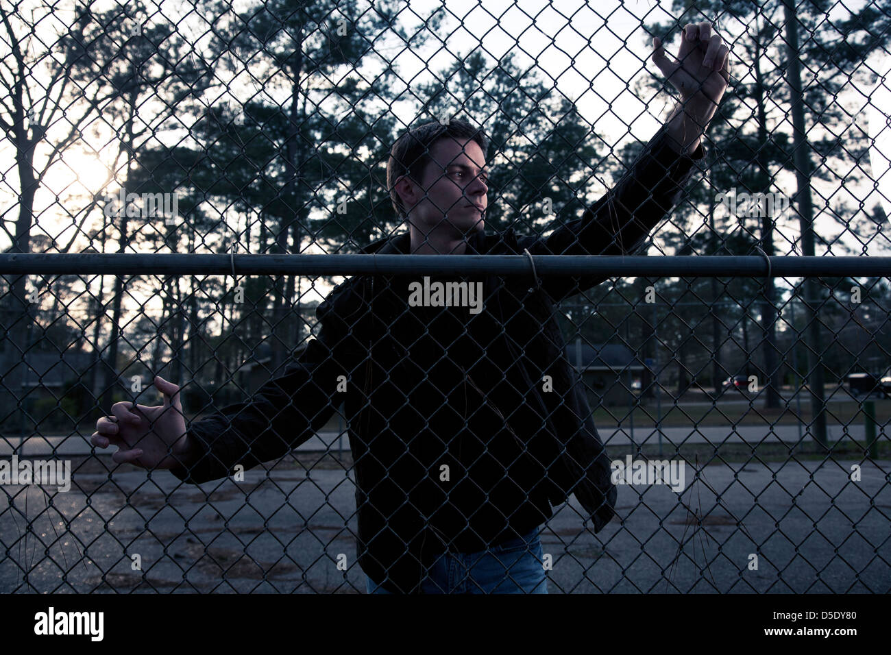 Man standing behind fence with sunset behind him Stock Photo - Alamy