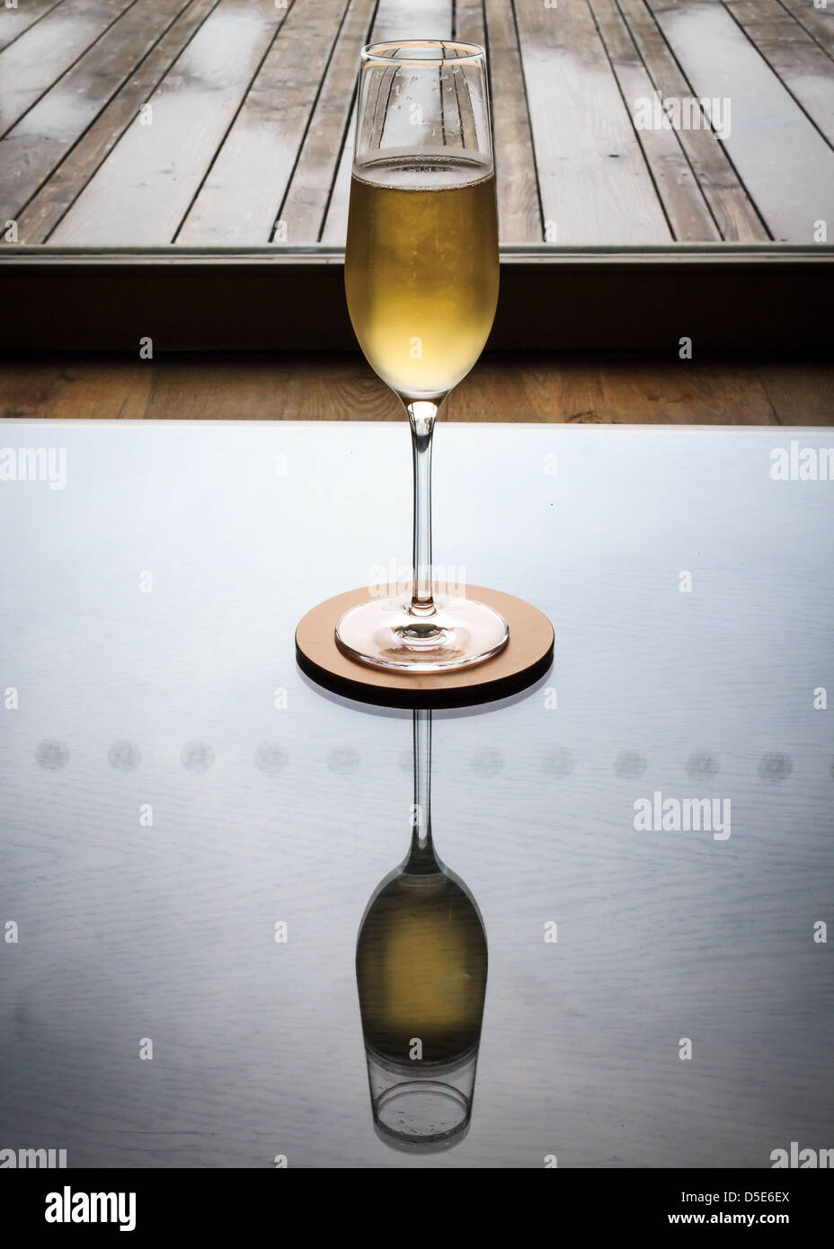 A single Champagne glass sits on a highly polished table, which shows ...