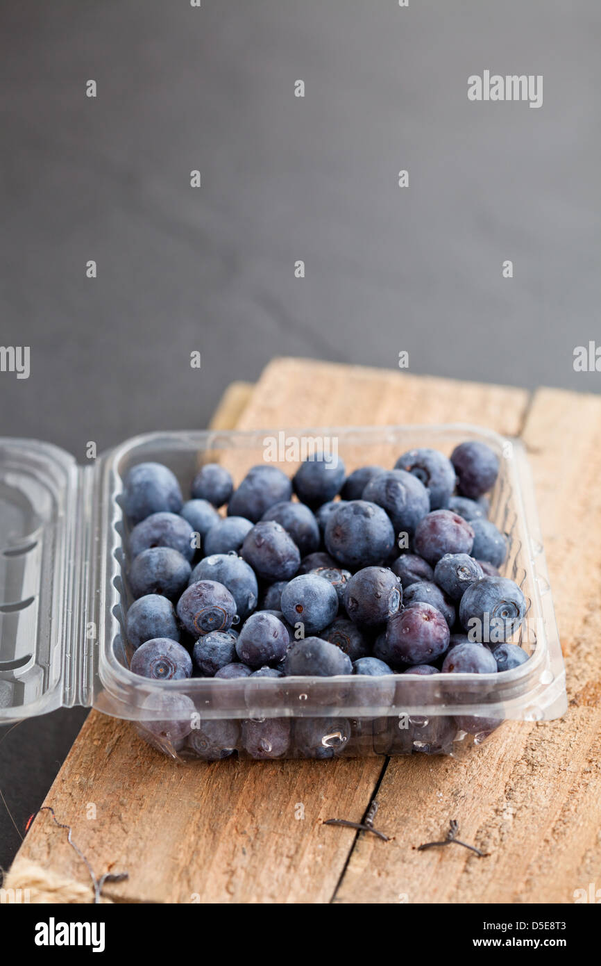 Closeup of fresh blueberries in plastic container resting on wooden ...