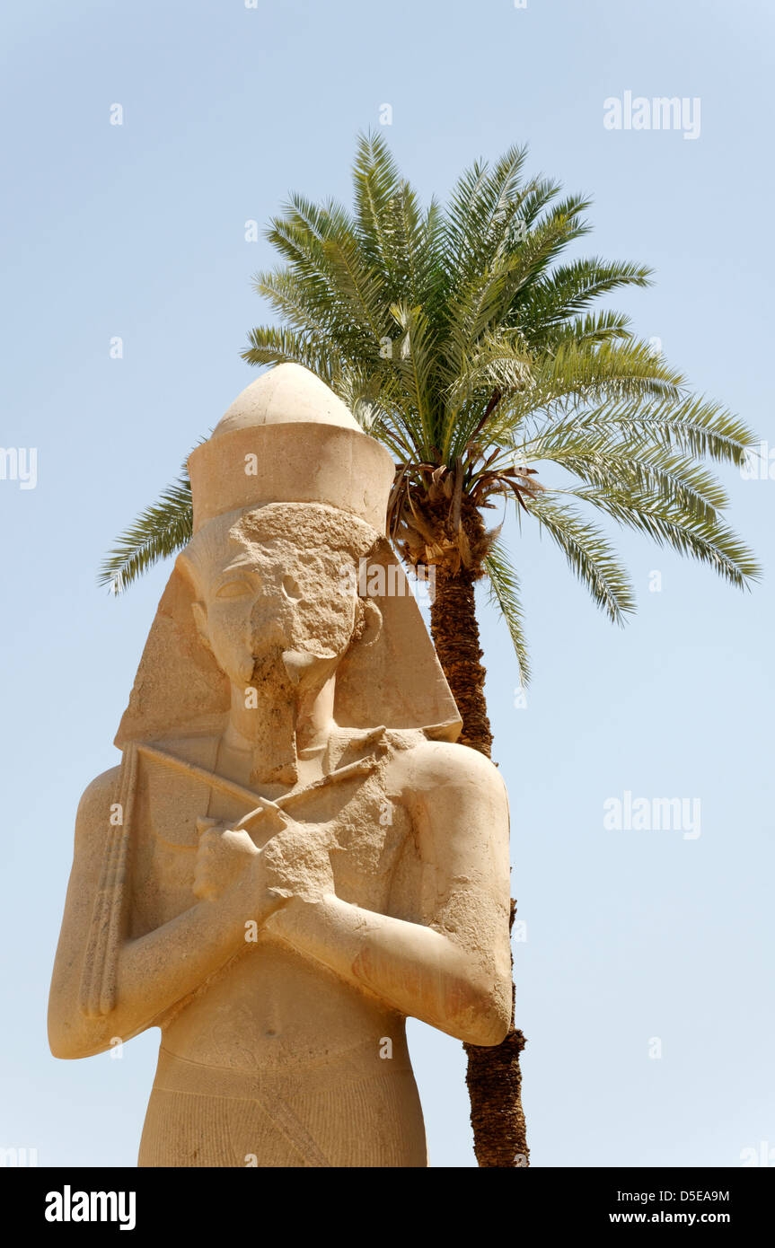 Luxor. Egypt. Palm tree shades a granite statue of Ramses II, at the ...