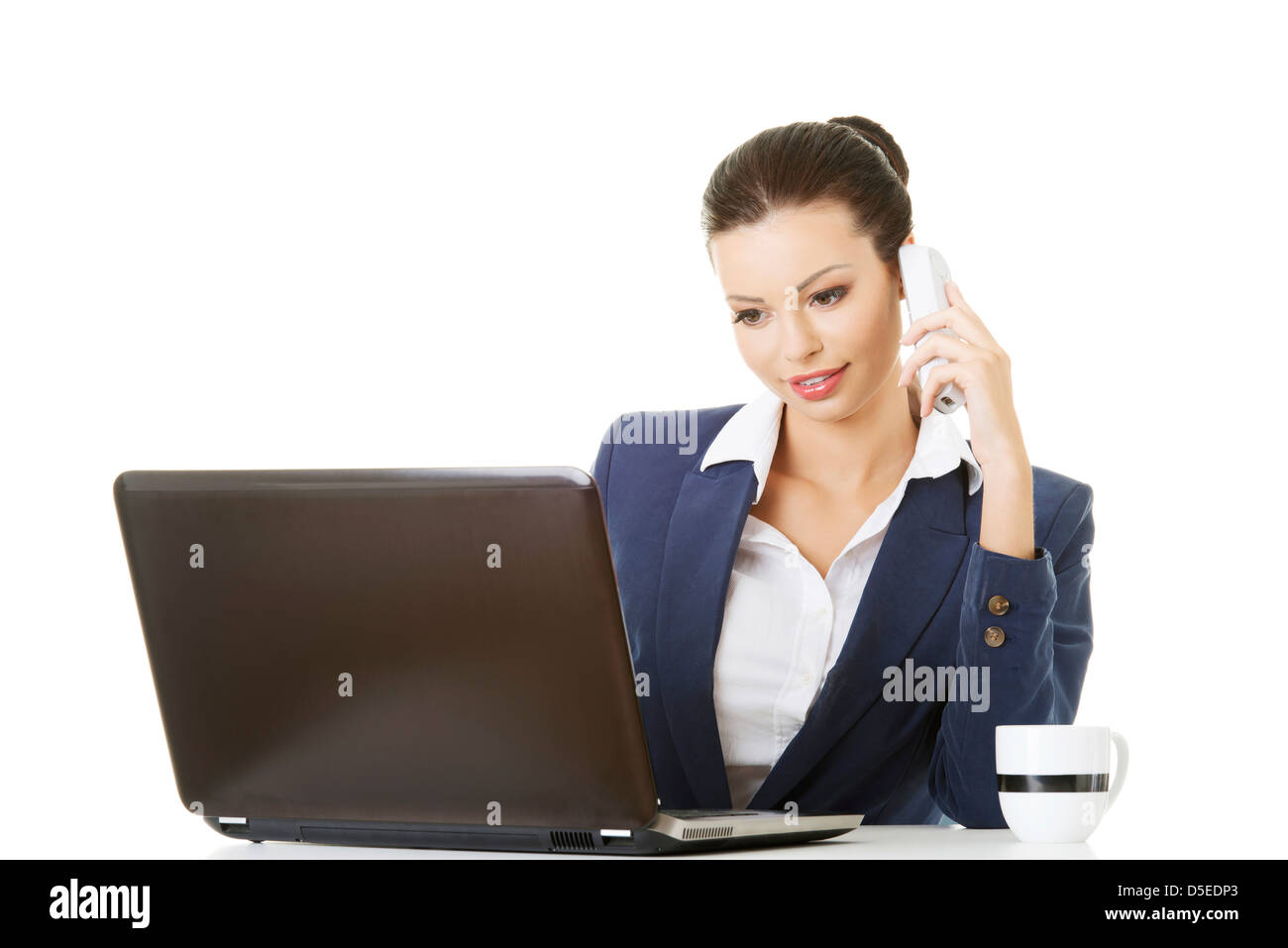 Smiling young business woman speaking on phone while using laptop ...