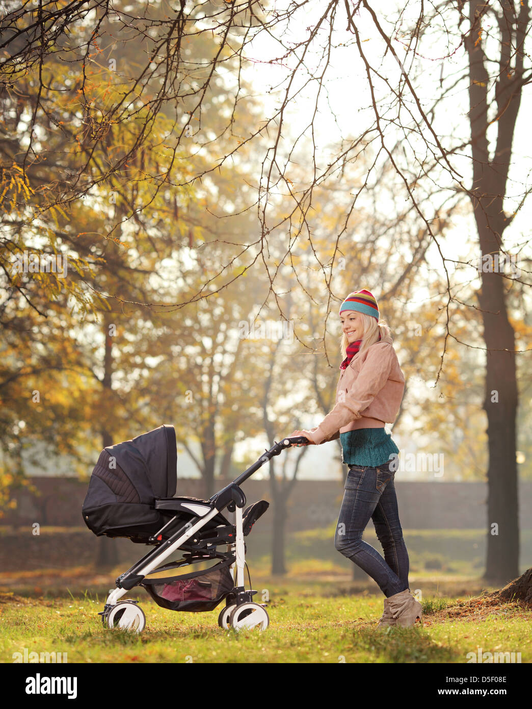A smiling mother posing with a baby stroller in a park in autumn, shot ...