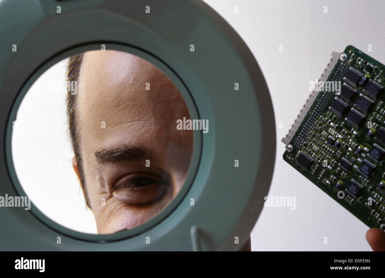 Technician looking through magnifying glass holding electrical circuit ...