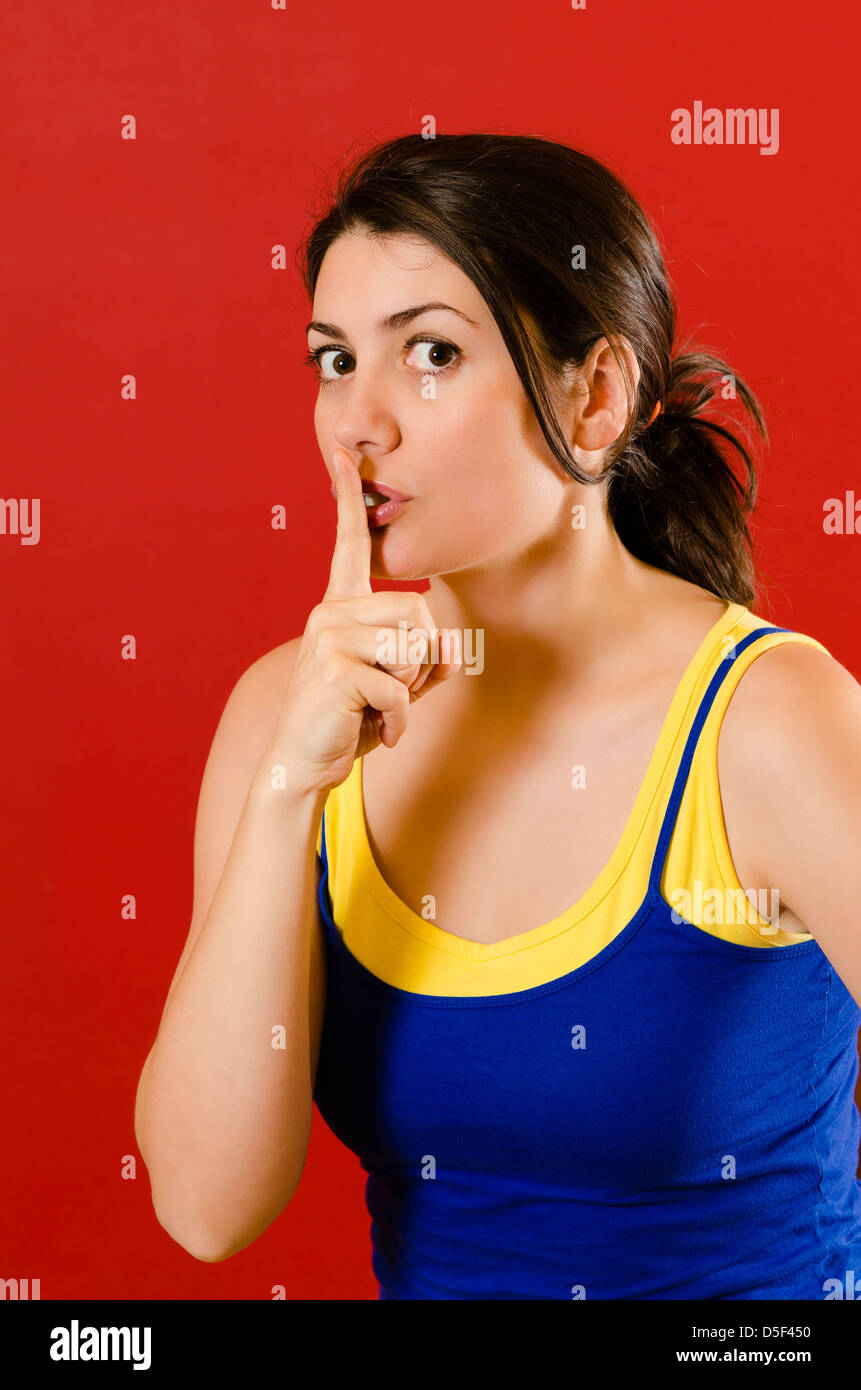 Young woman making a hush gesture on red background Stock Photo - Alamy