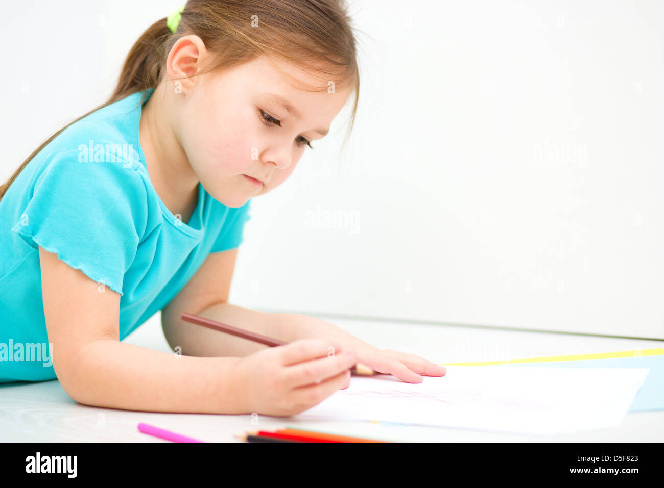 Little girl is drawing using color pencils while laying on floor Stock ...