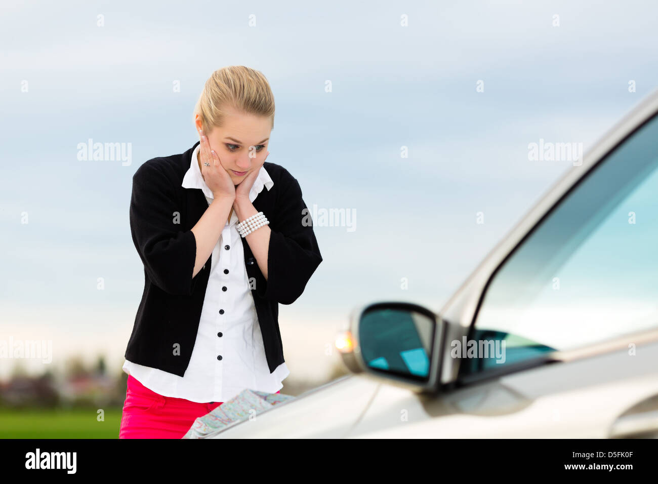 Young woman in front of bonnet of a car with map looking for directions ...