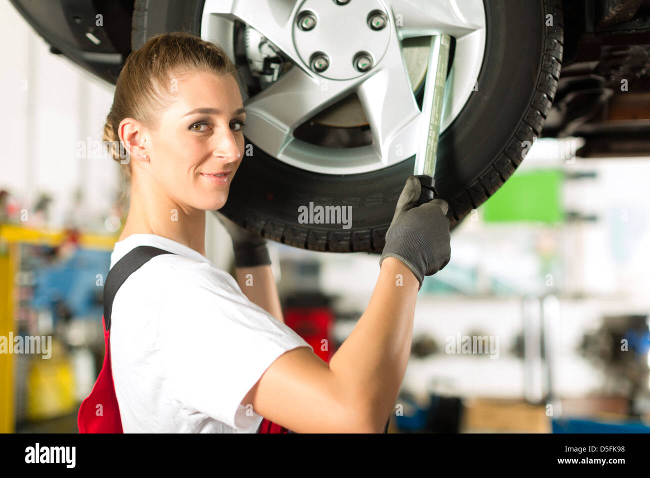 Young woman as female car mechanic working on an auto in workstation ...