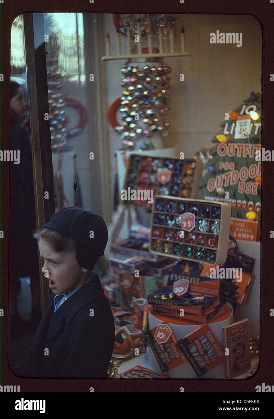 This 1940s photograph features a boy standing beside a store window ...