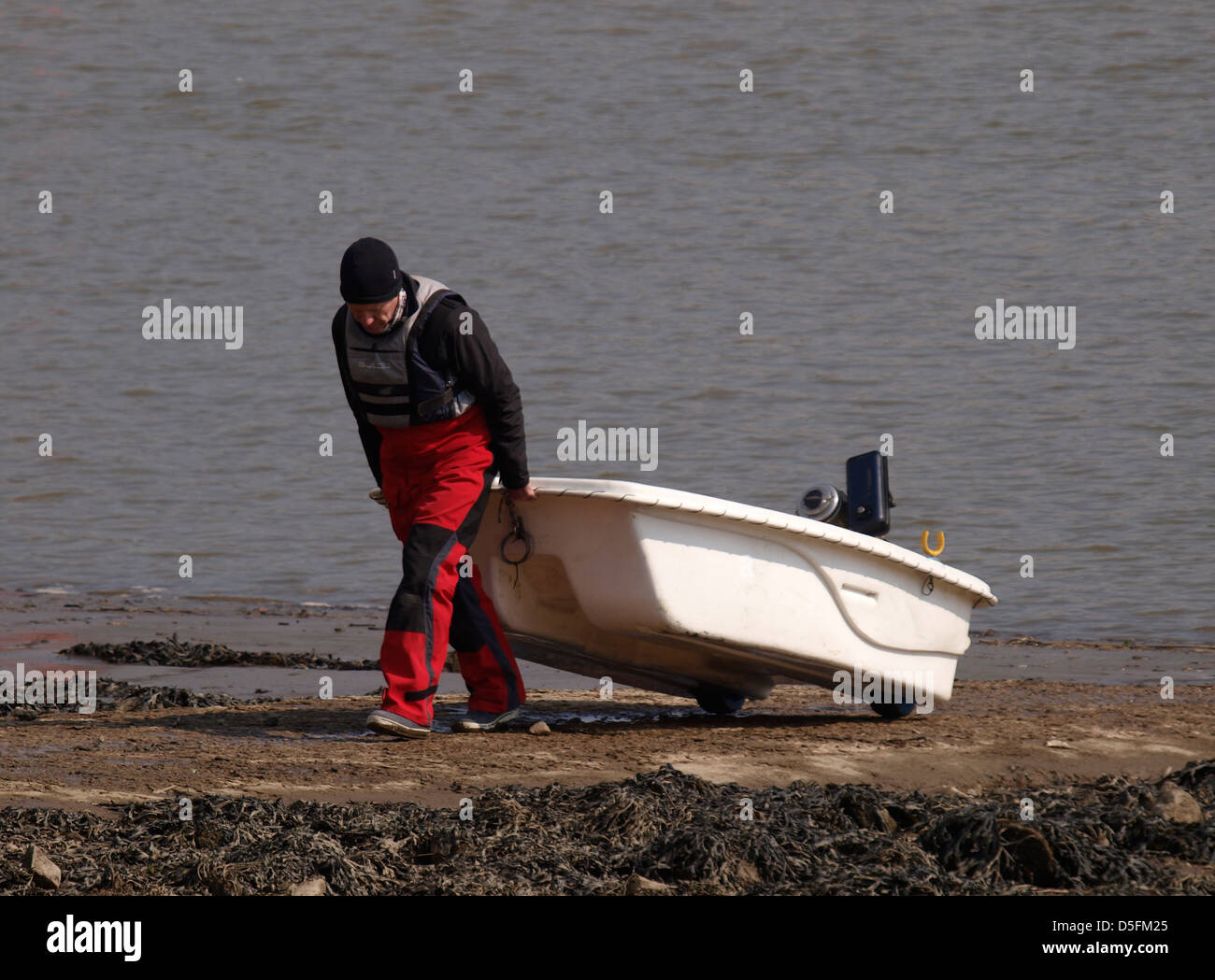 Man pulling a dinghy with wheels up slipway, Saltash, Cornwall, UK 2013 ...