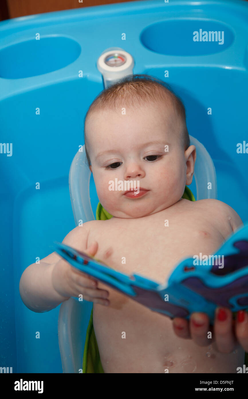 A five month baby sitting in a bath tube looking at a baby's book Stock Photo - Alamy