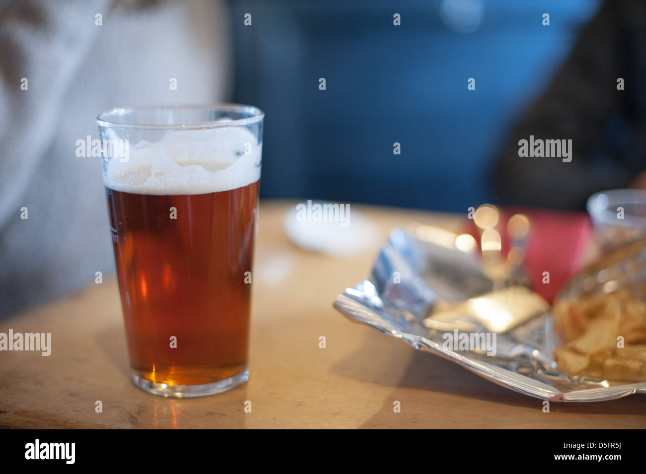 Partly drunk pint of lovely looking golden beer and a packet of open ...