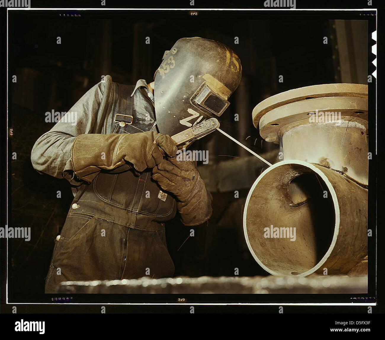 This photograph from 1942 shows a welder working on ship boilers at the ...