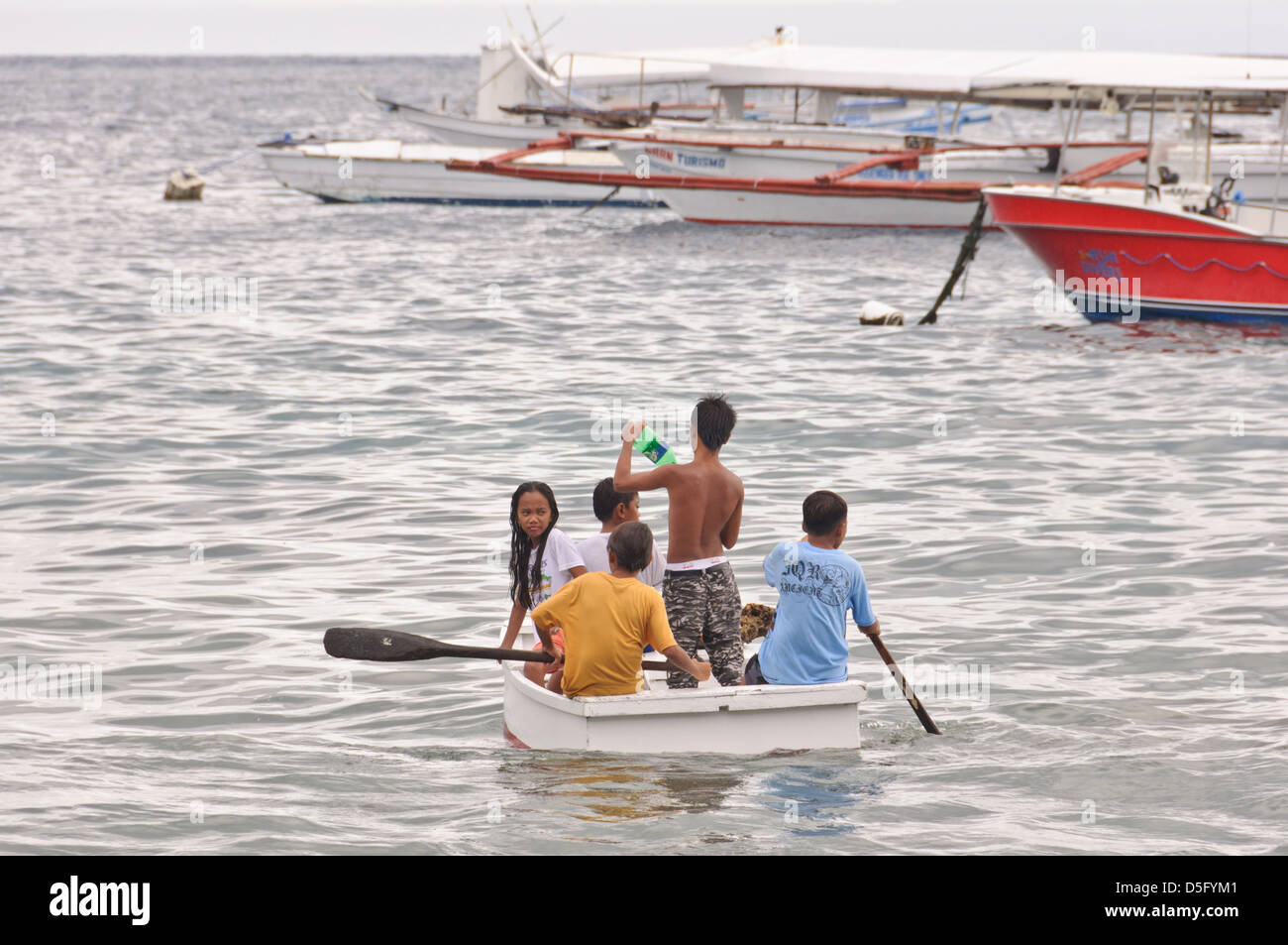 5 Asian children, 1 girl, 4 boys, rowing in a small boat on the ocean ...