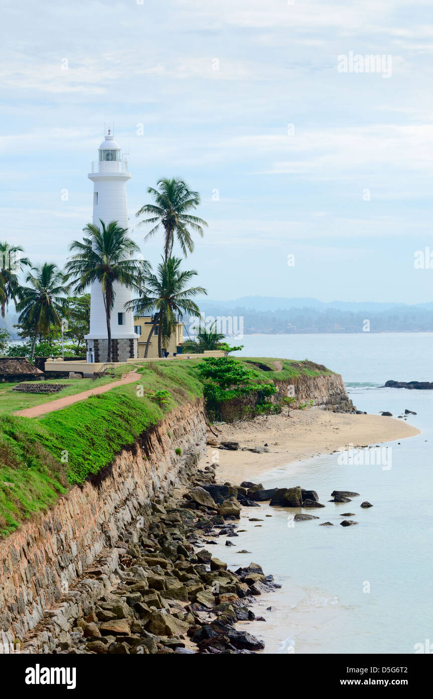 White lighthouse on fortified stone wall with cloudy sky background ...