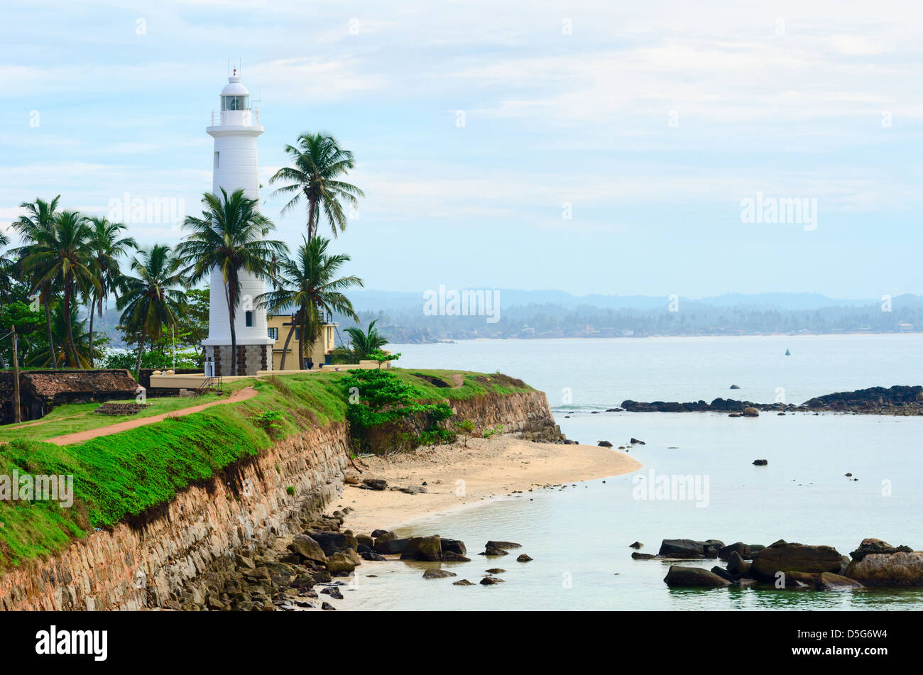 White lighthouse on fortified stone wall with cloudy sky background ...