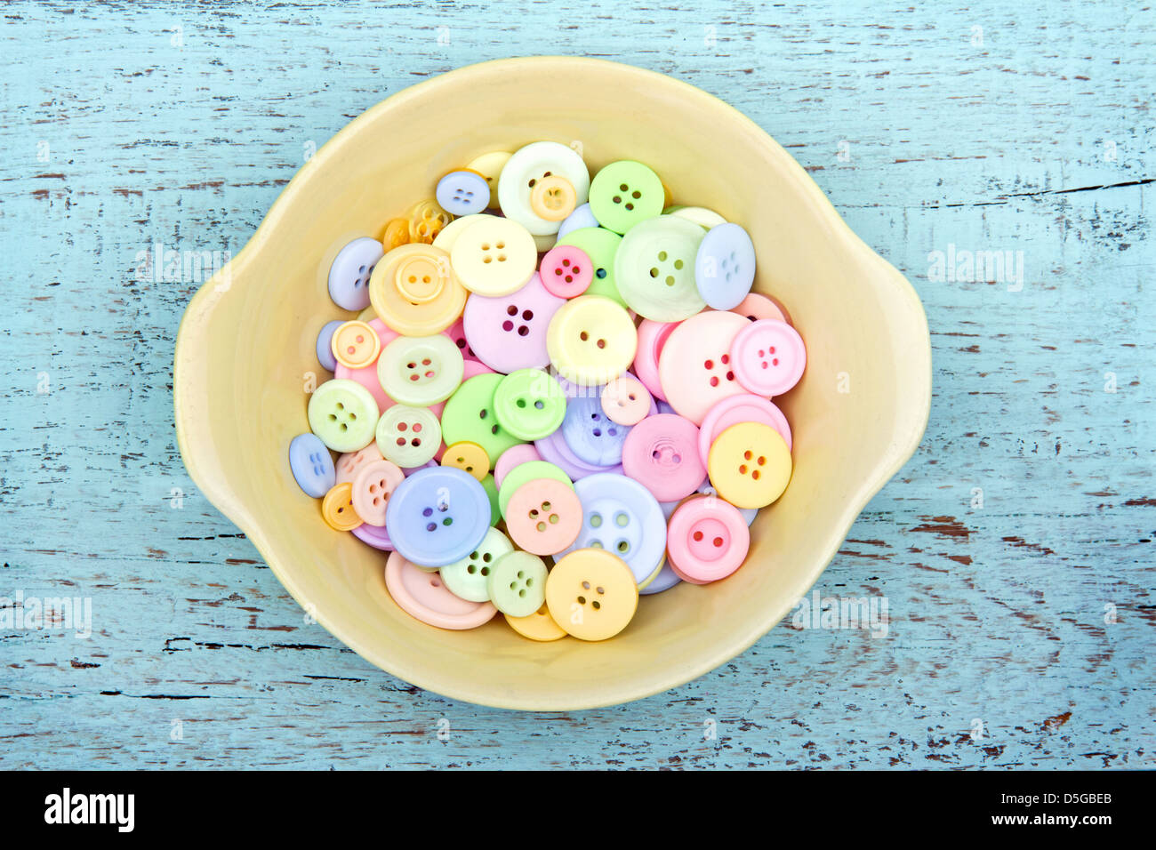 Pastel color buttons in a yellow bowl on vintage wooden background ...