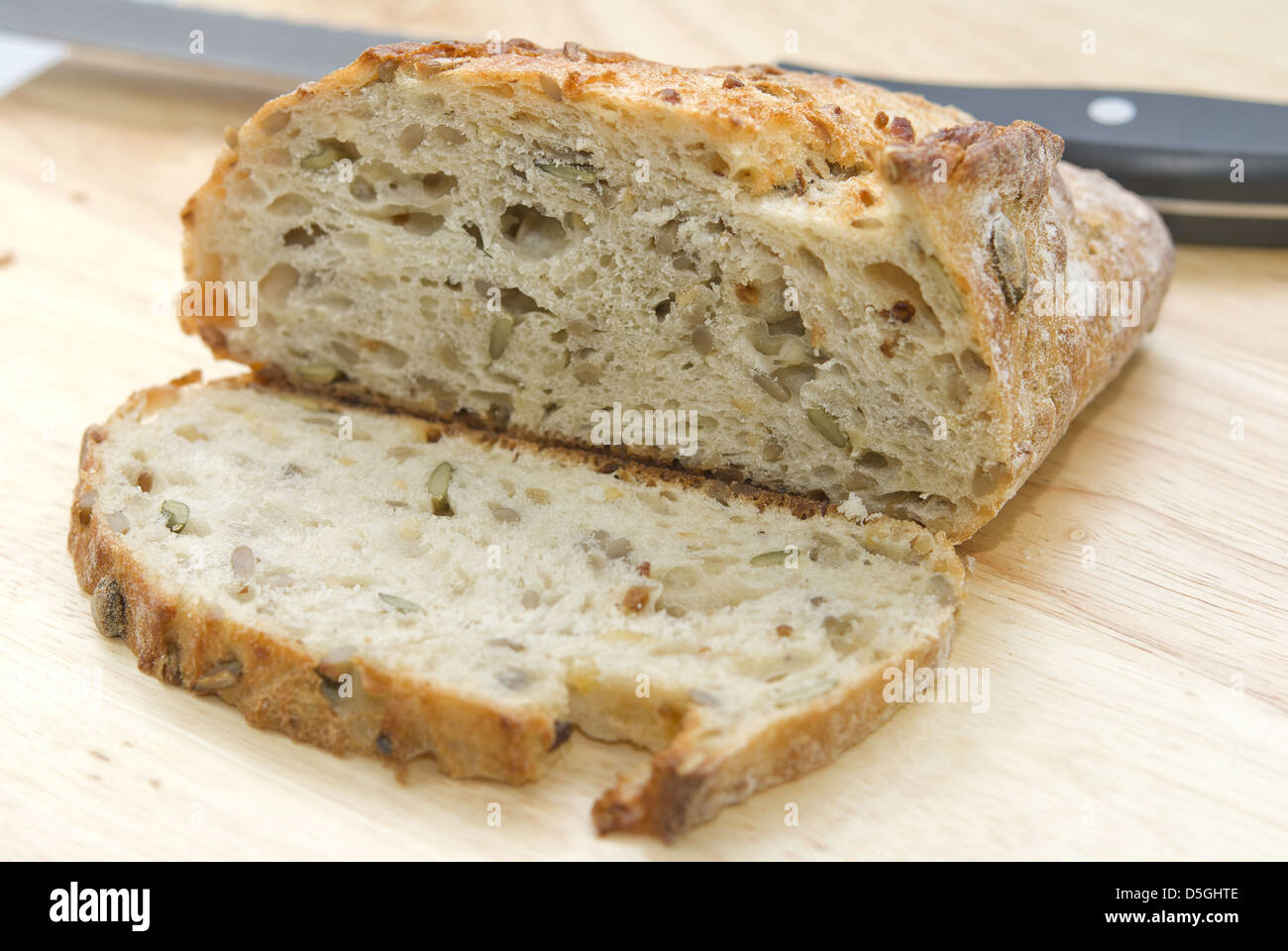 Loaf of bio bread with different seeds on the wooden table, knife in ...
