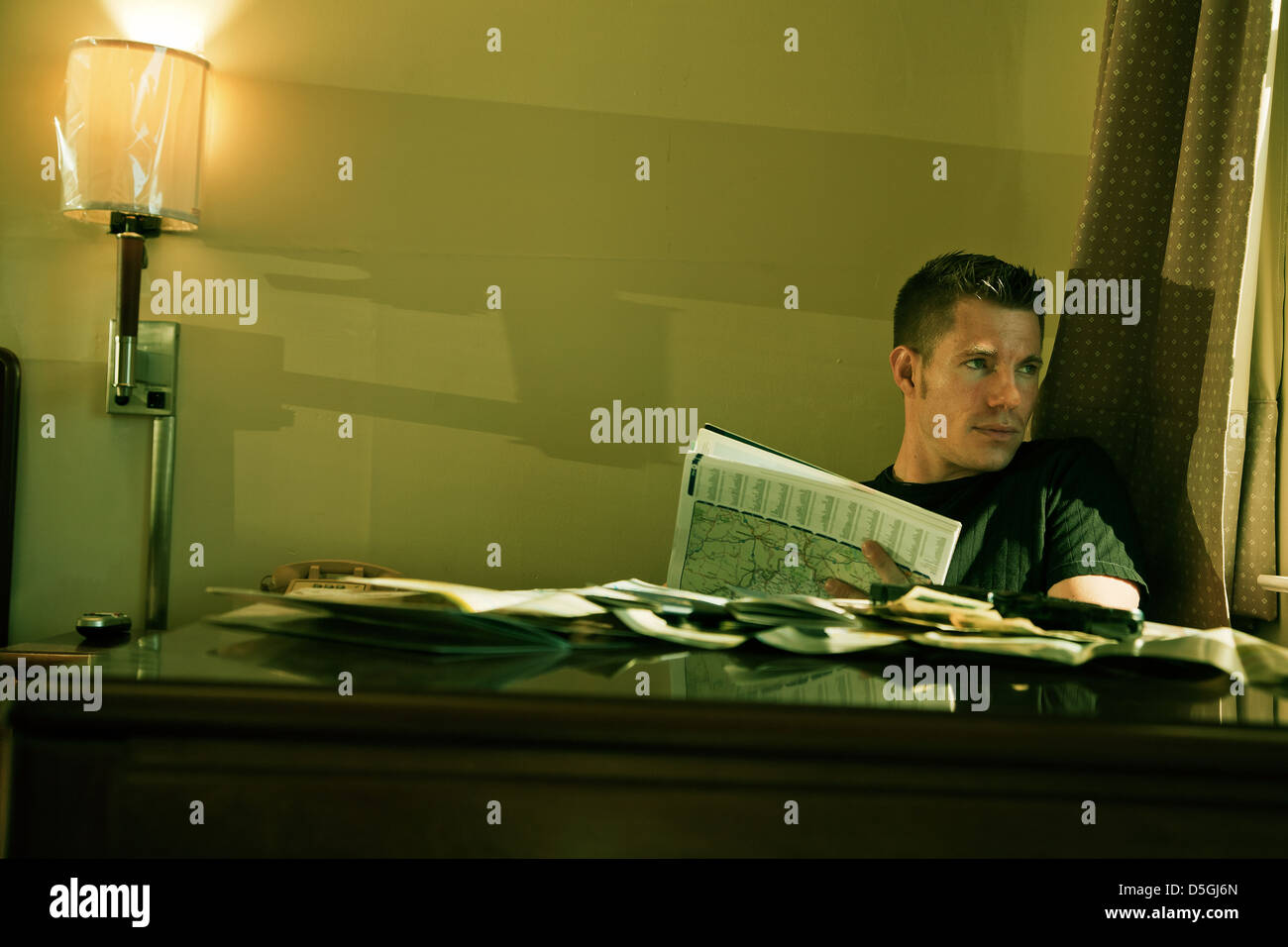 Man at desk looking out window reading map Stock Photo - Alamy