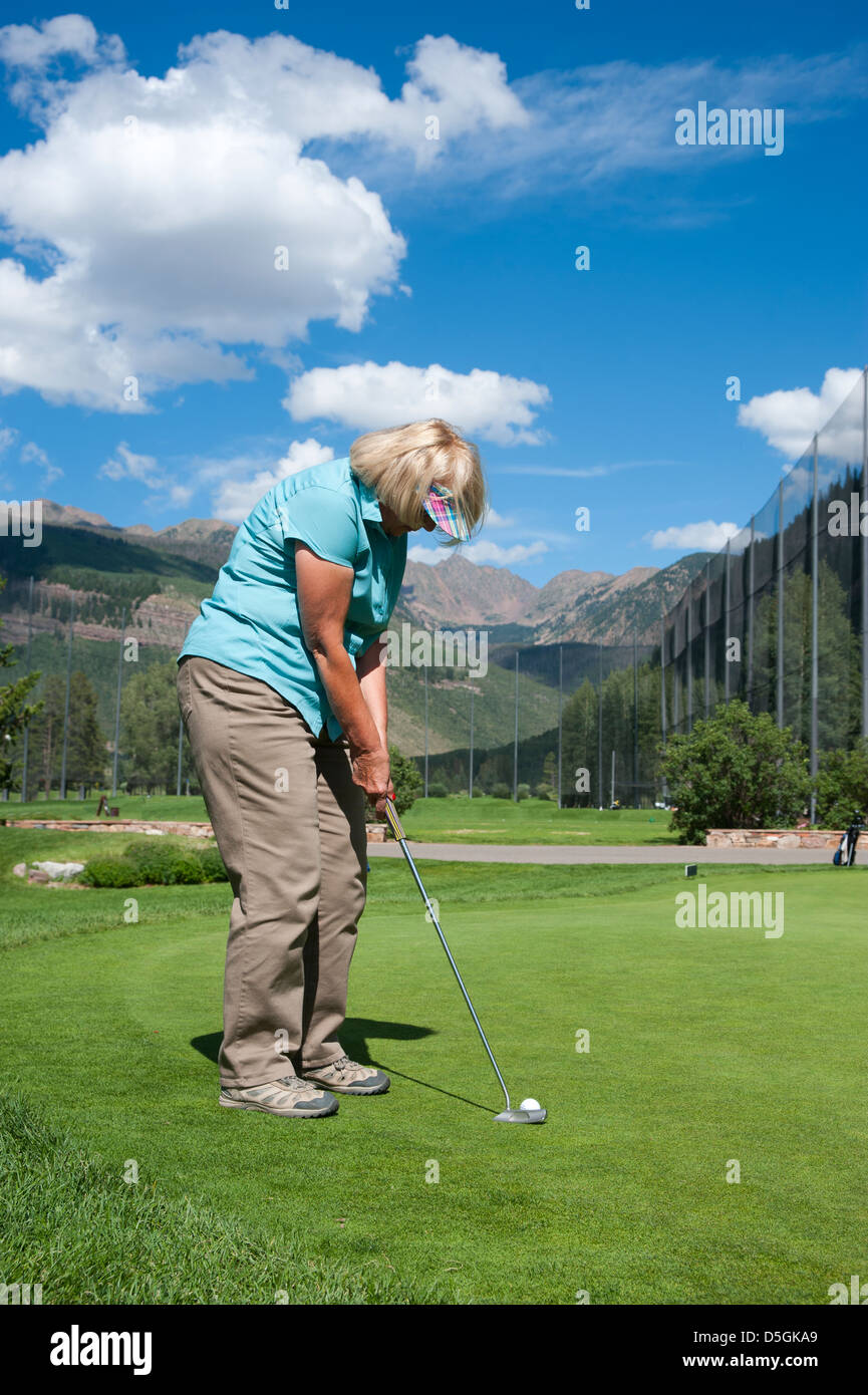 A female senior citizen practices her golf game on the putting green on ...