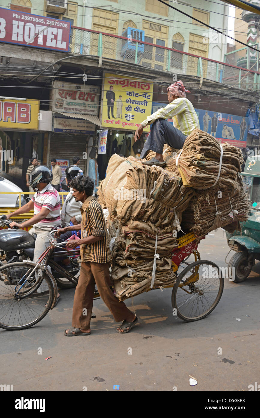 A sack merchant sitting high up on a pile of folded sacks on a rickshaw ...