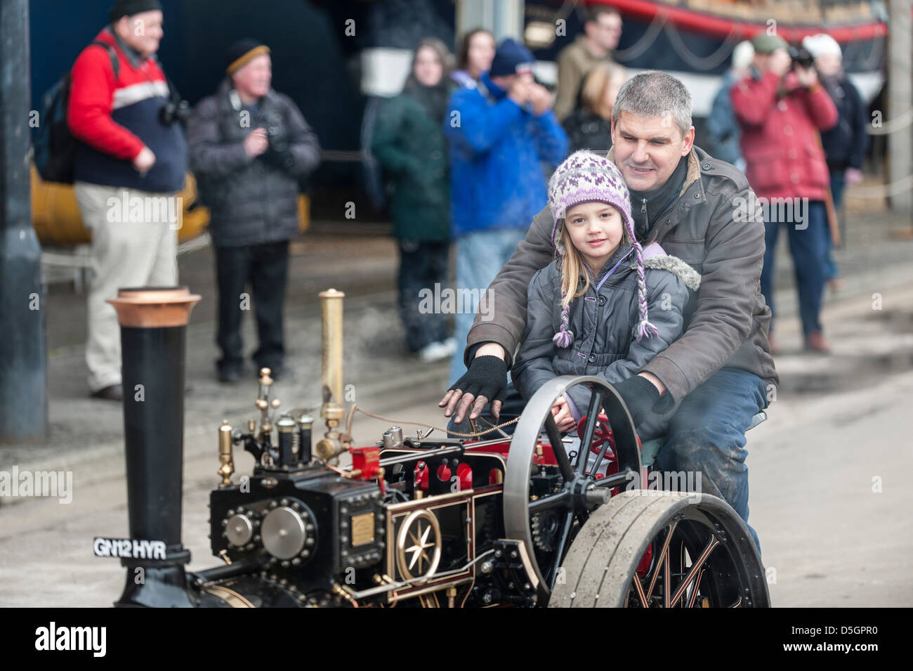 A father and his daughter riding on a miniature steam driven traction ...