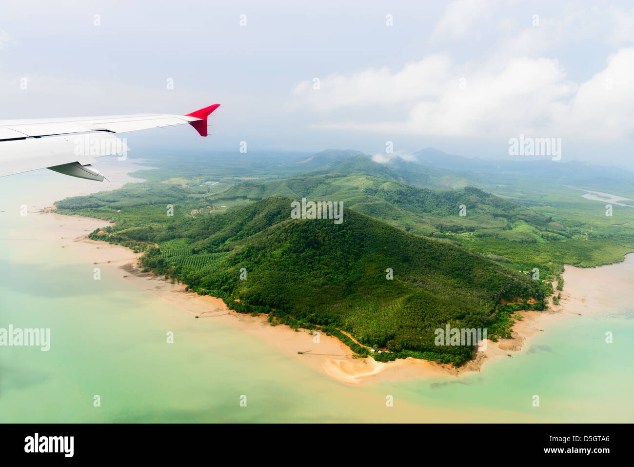 Aerial view of the tropical shore covered by green trees under airplane ...