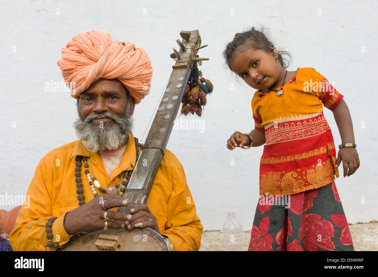 Musician holding a sitar with his young daughter dancing at the Pushkar ...