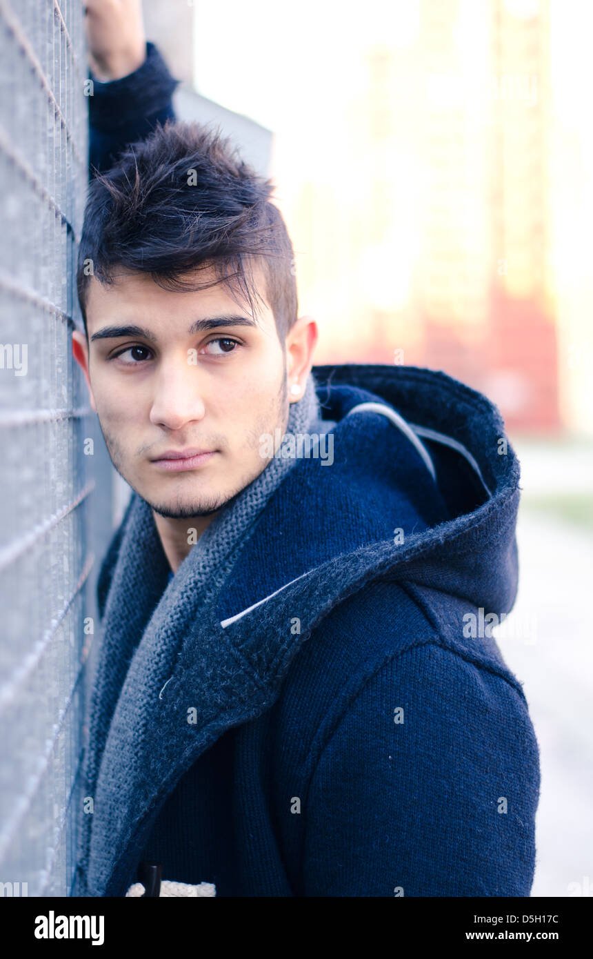 Good looking young man leaning against metal grid, urban setting and ...