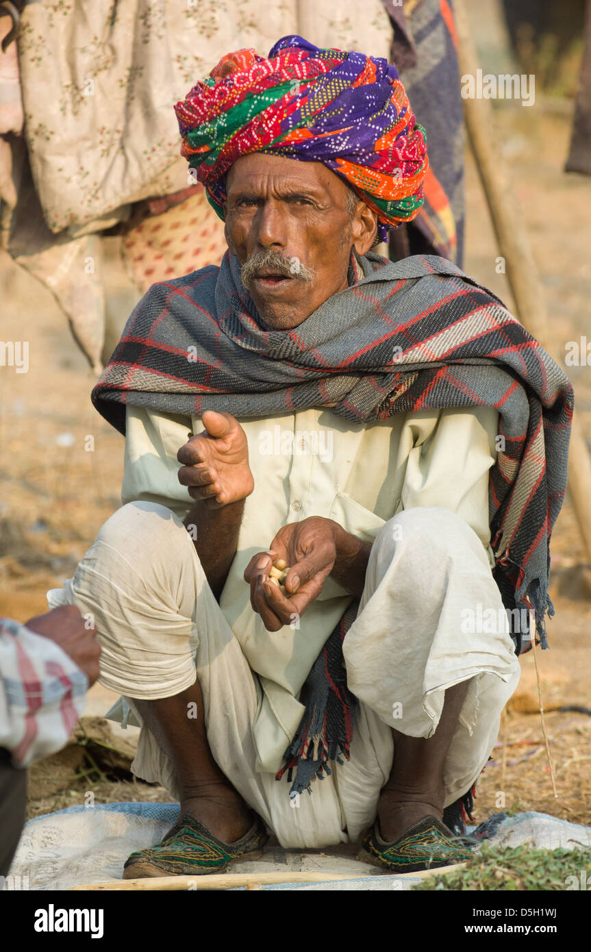Man with a multicoloured turban squatting whilst eating nuts at the ...