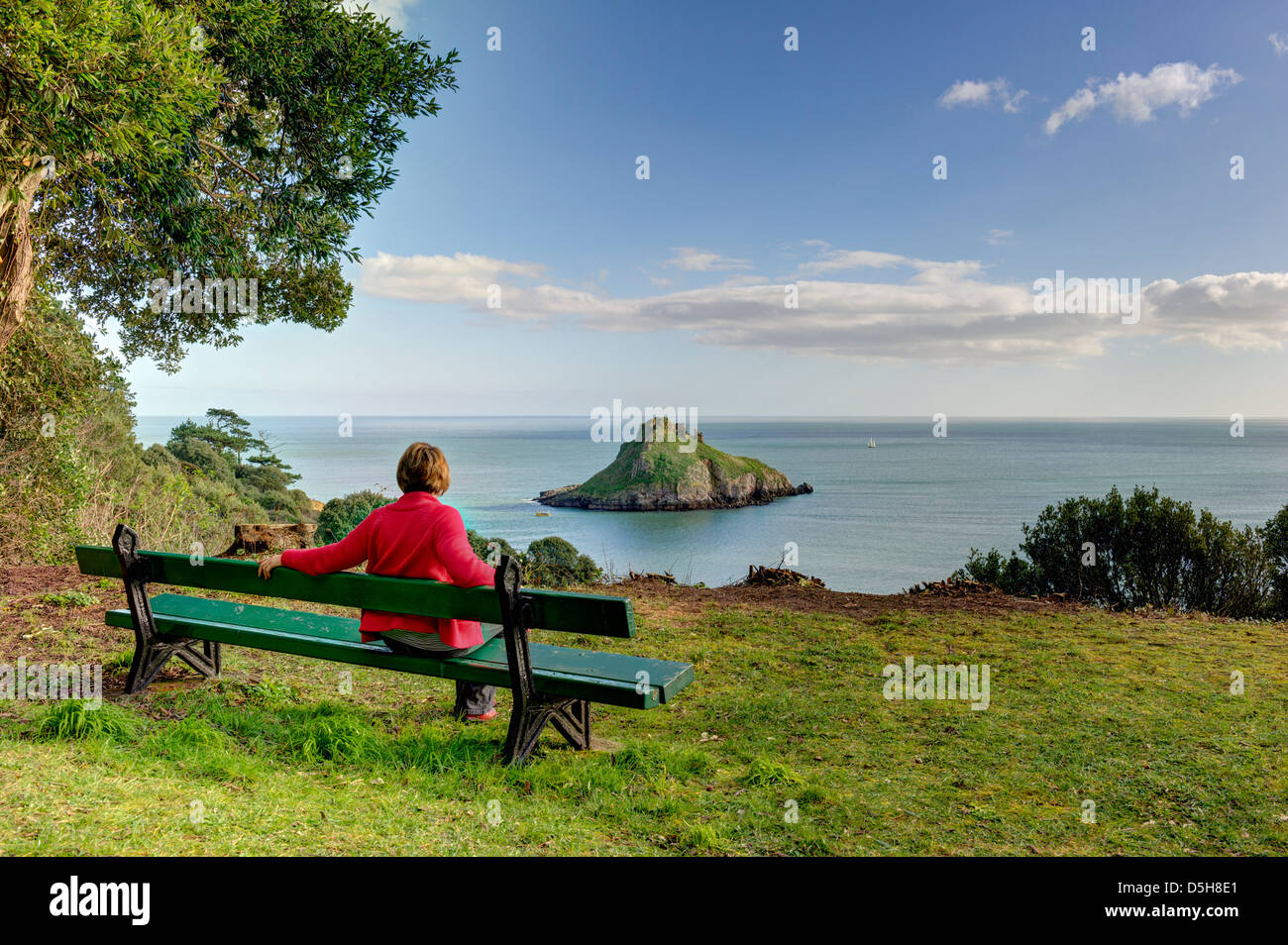 Woman in red relaxes on a bench overlooking view of Thatcher Rock, a ...