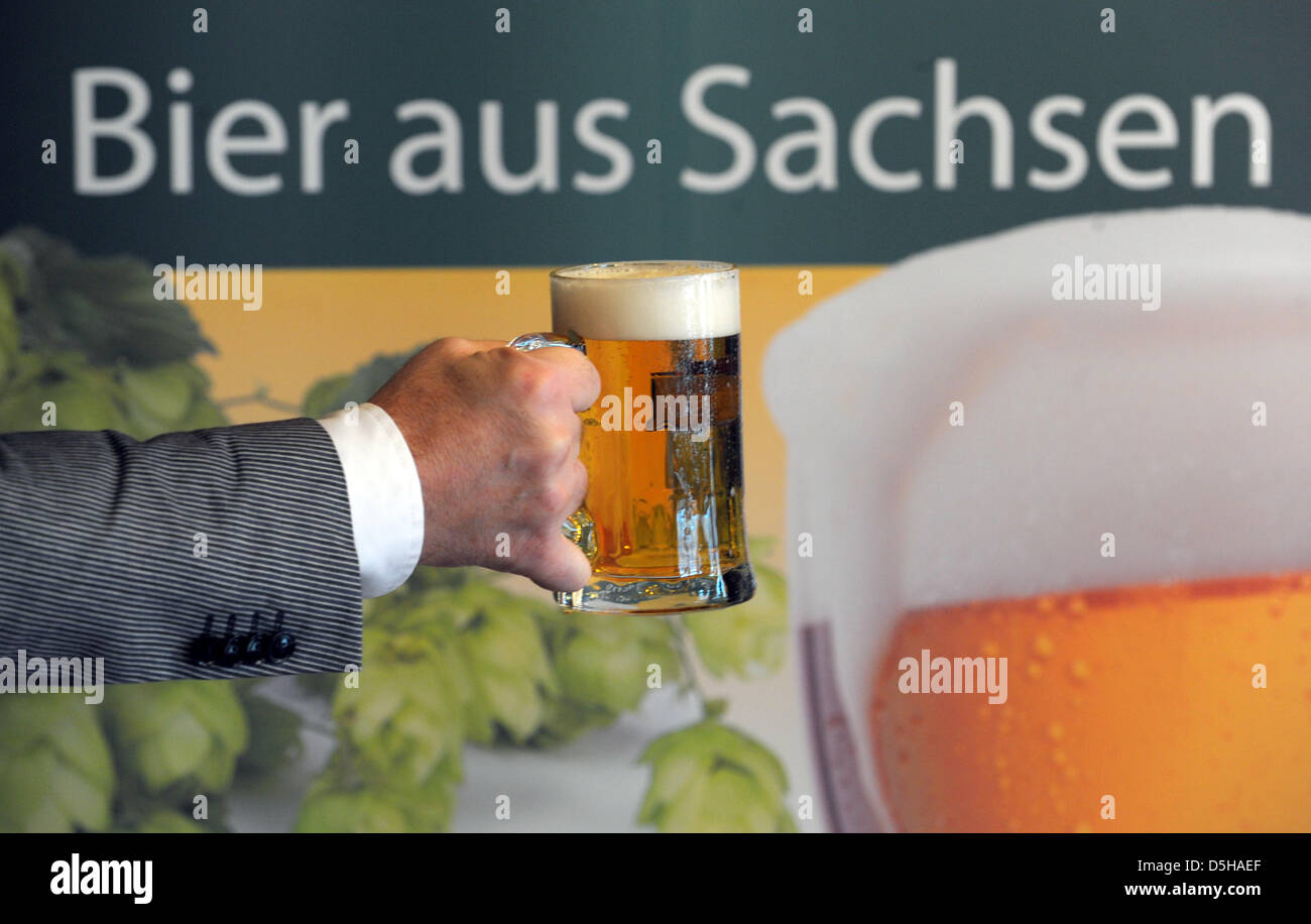 A full glass of beer is held in front of a promotional poster for beer ...