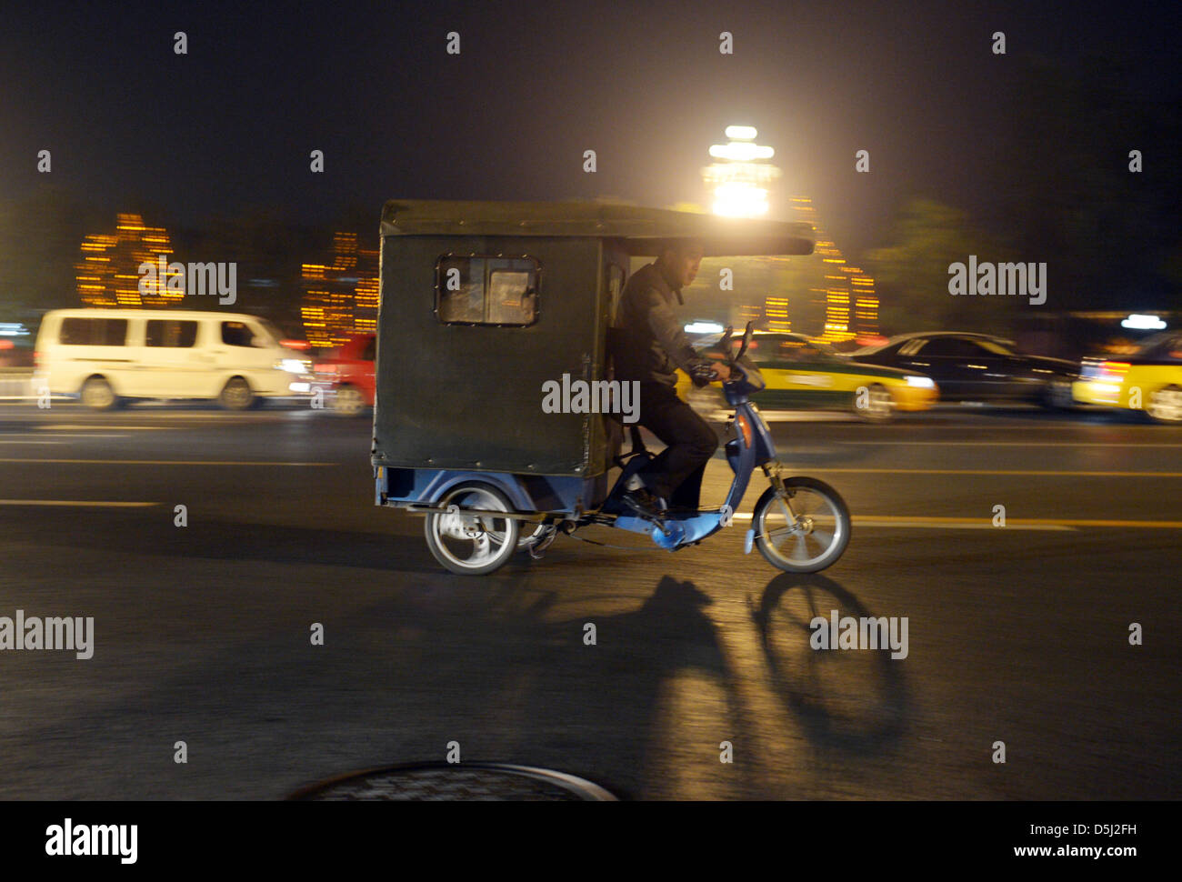 A man rides on a tricycle through busy evening traffic in Bejing, China ...