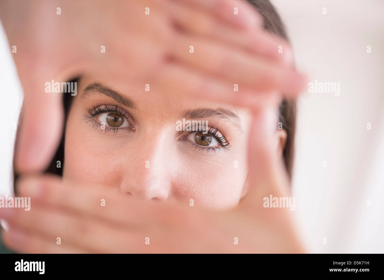 Woman looking at camera through handsframe Stock Photo - Alamy