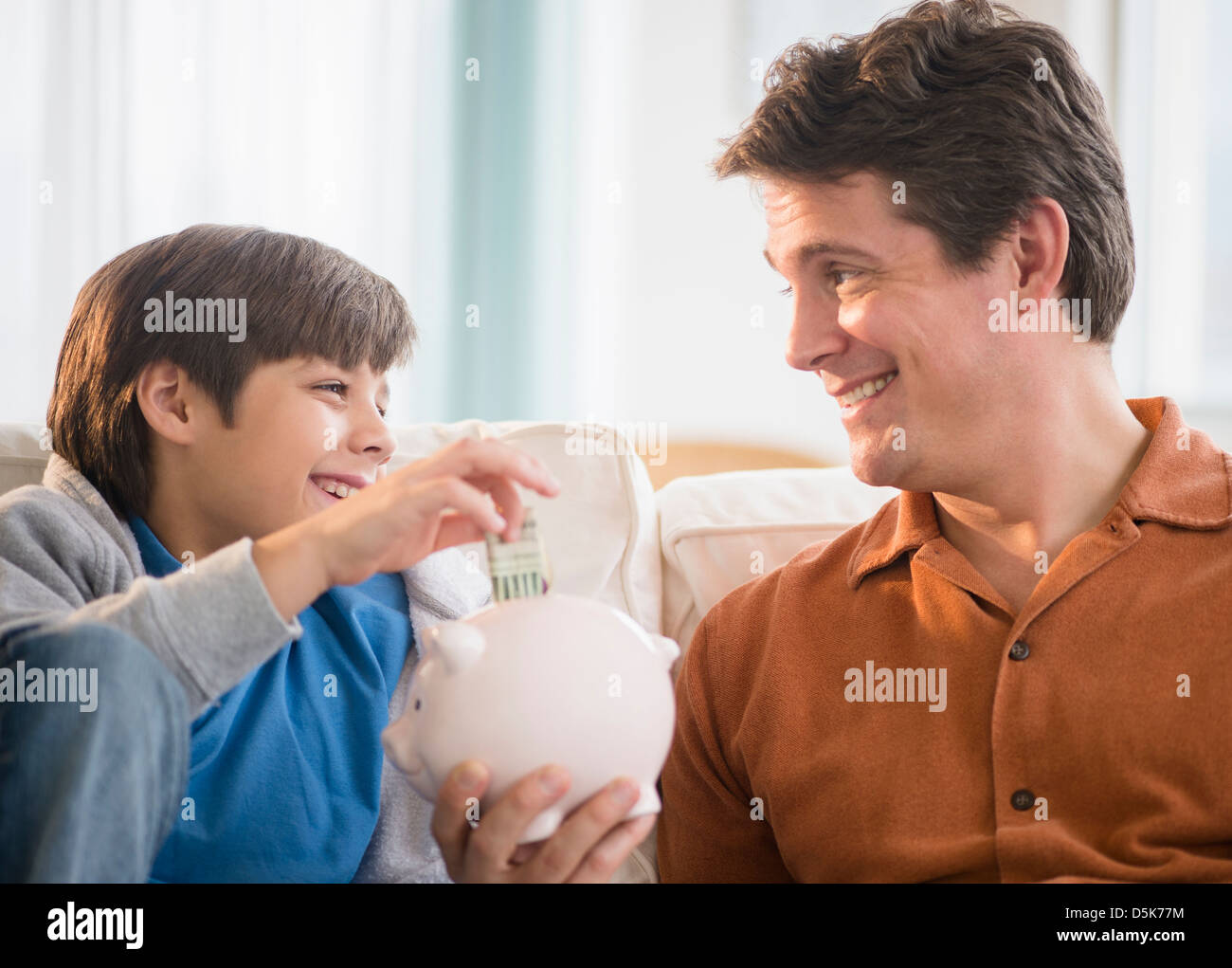 Father and son (8-9) putting money into piggybank Stock Photo - Alamy