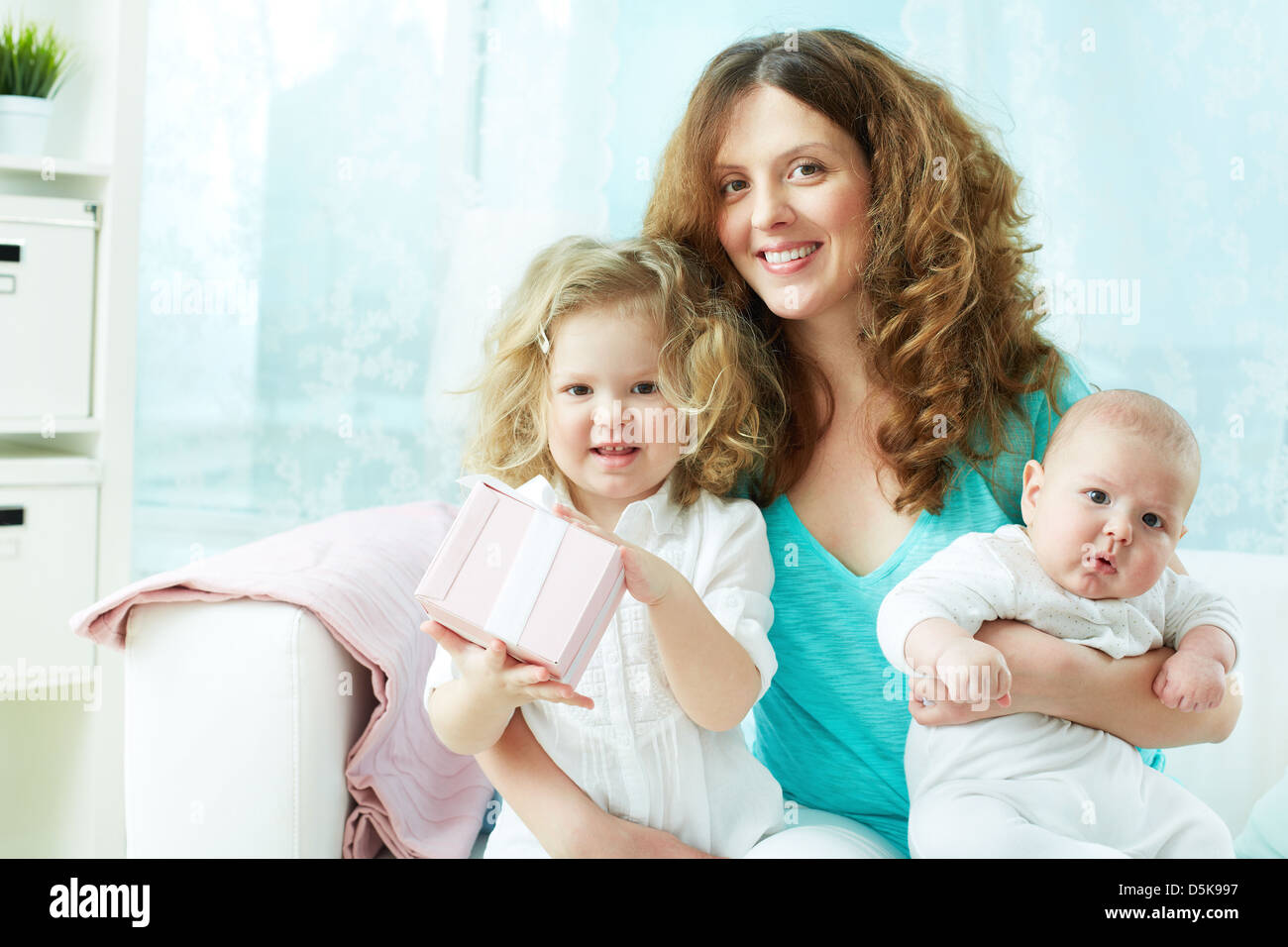 Happy mother giving her children a hug, her daughter holding a gift-box ...