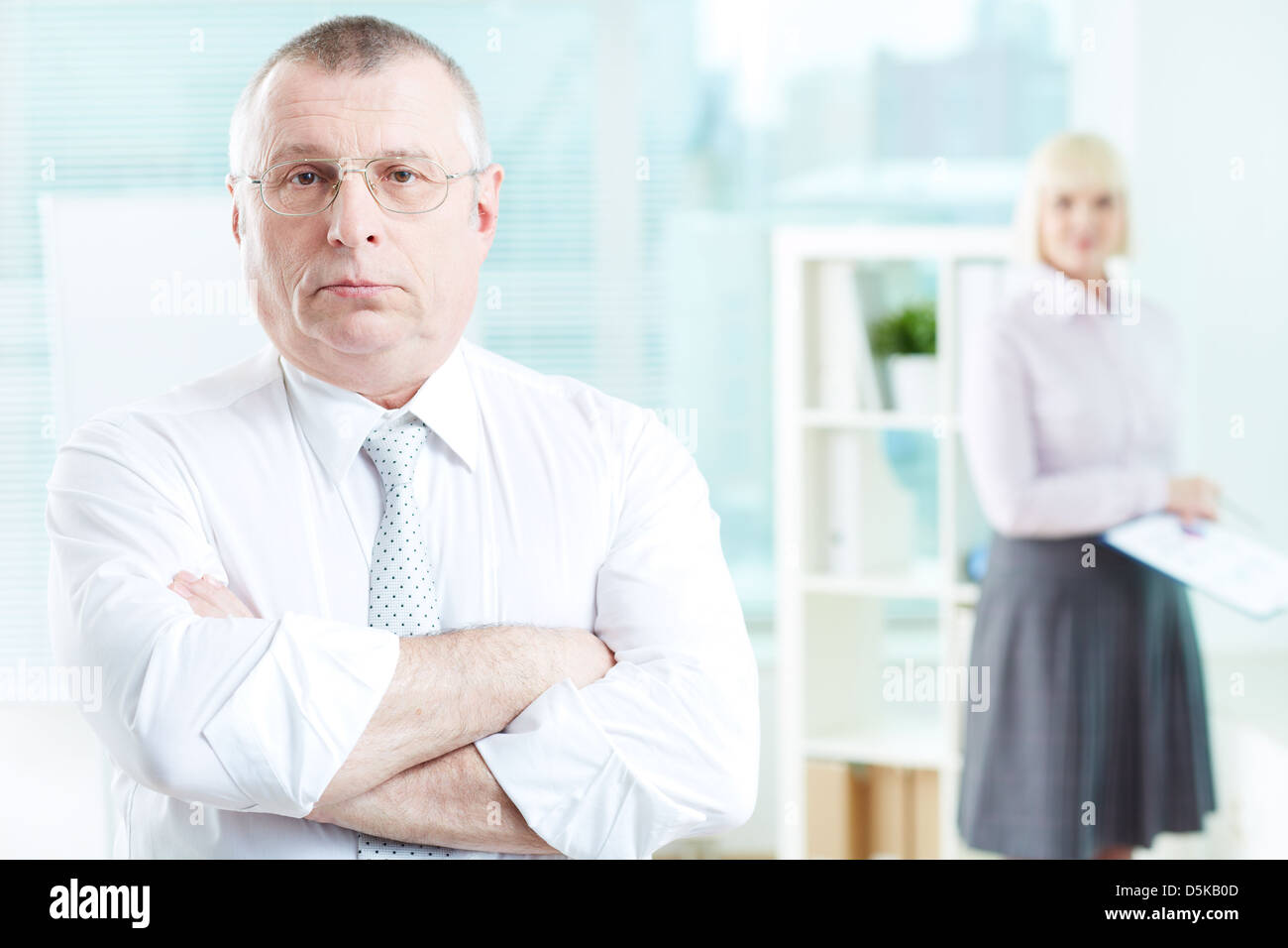 Portrait of serious boss looking at camera with female standing on ...