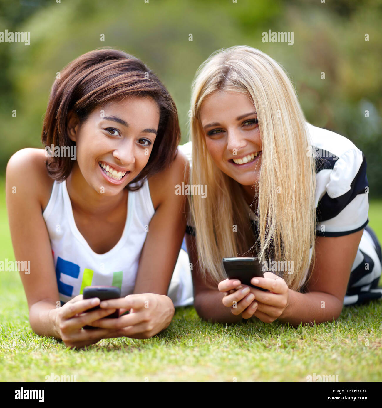 Portrait of young women lying on grass, using mobile phone Stock Photo ...
